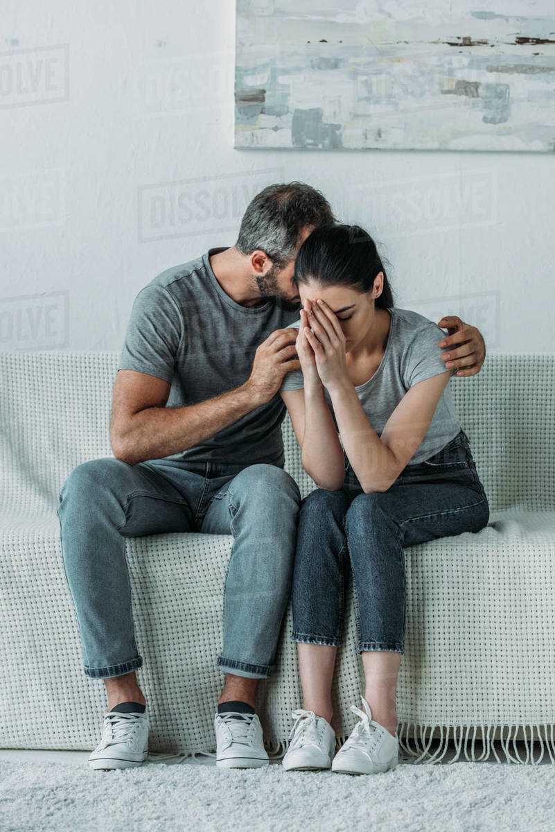 Upset young man supporting depressed girlfriend while sitting together ...