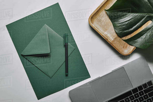 Green paper for letter template by laptop on white marble background ...