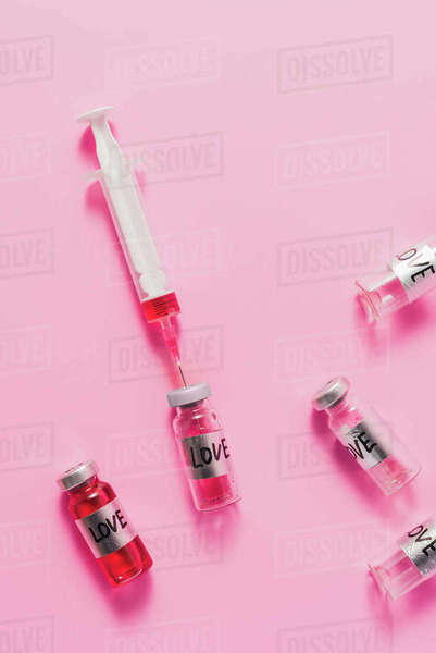 Top view of syringe and bottles with love vaccine signs on pink surface ...