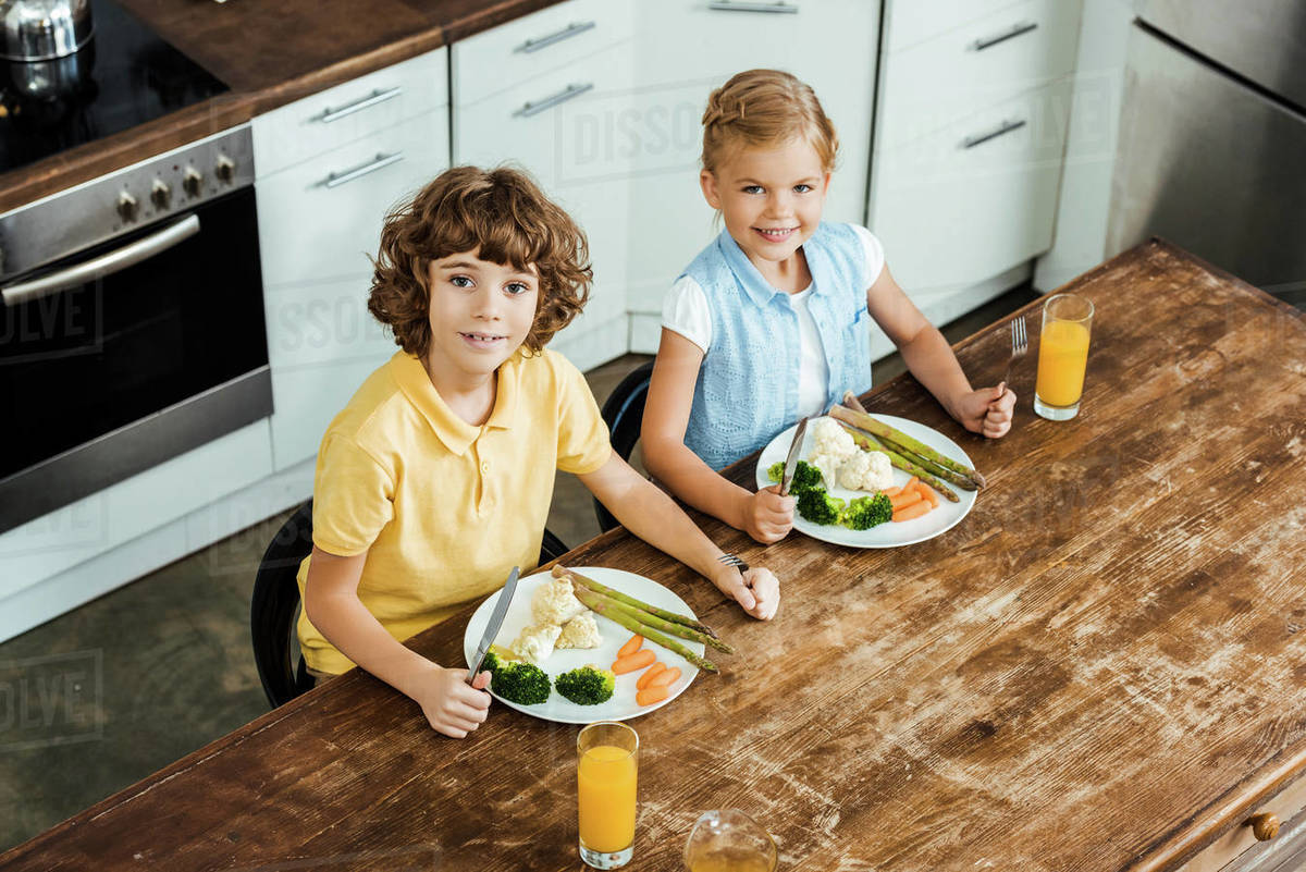 High angle view of cute happy children eating healthy vegetables and ...