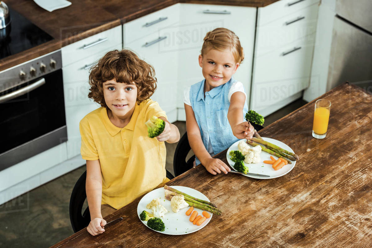 High angle view of happy cute children holding forks with broccoli and ...