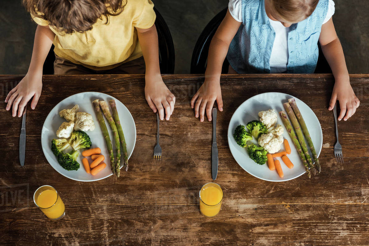 Cropped shot of cute little kids eating healthy vegetables at wooden ...