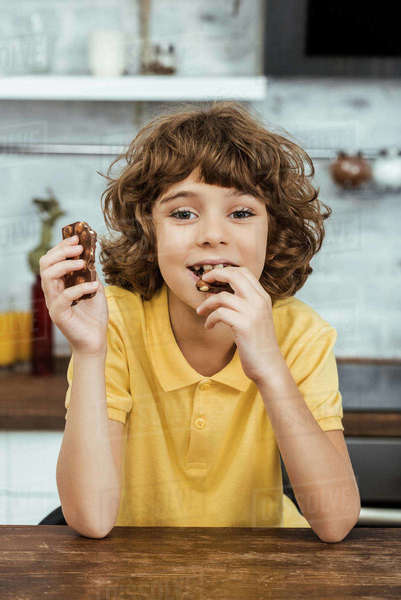 Cute happy boy eating delicious chocolate with nuts and smiling at ...