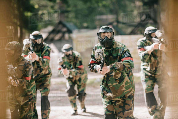 Selective focus of paintball team in uniform and protective masks ...