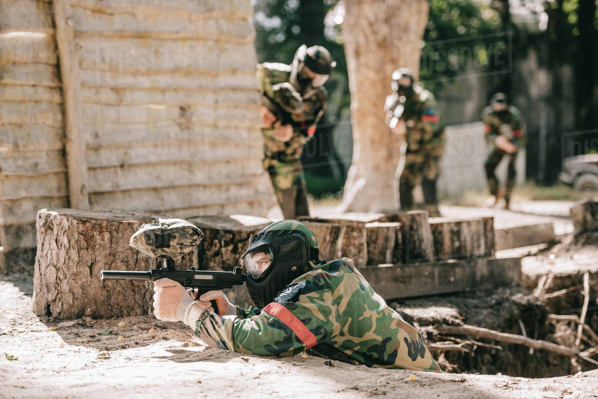 Selective focus of paintball player laying on ground and aiming with ...