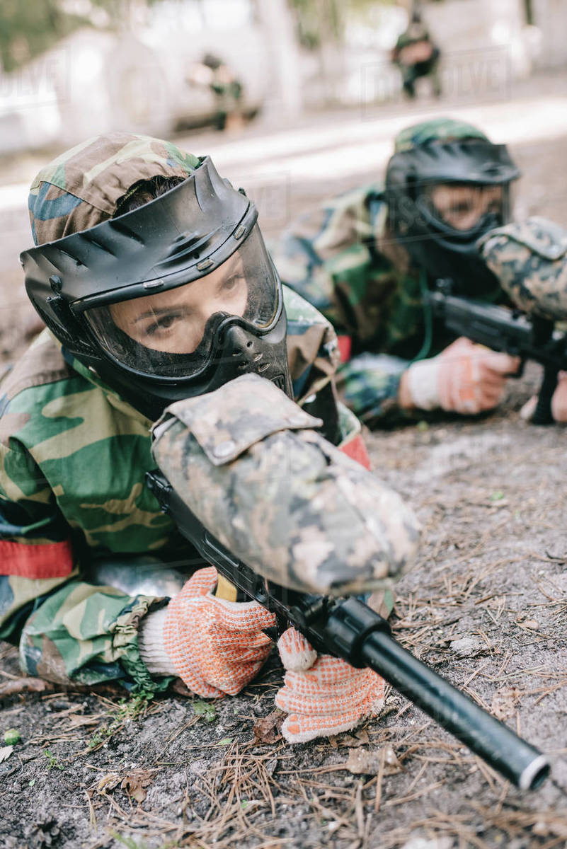 Female paintball player in goggle mask and camouflage with marker gun ...
