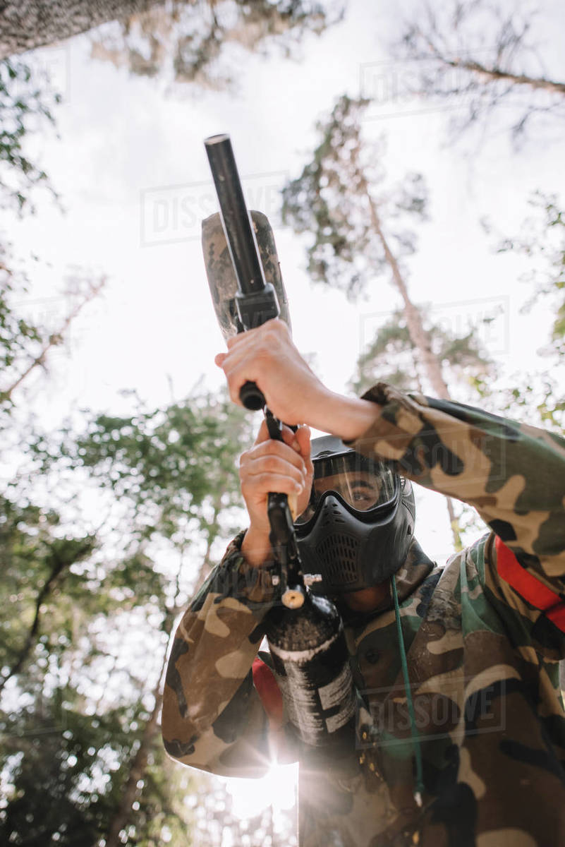 Low angle view of male paintball player in goggle mask and camouflage ...