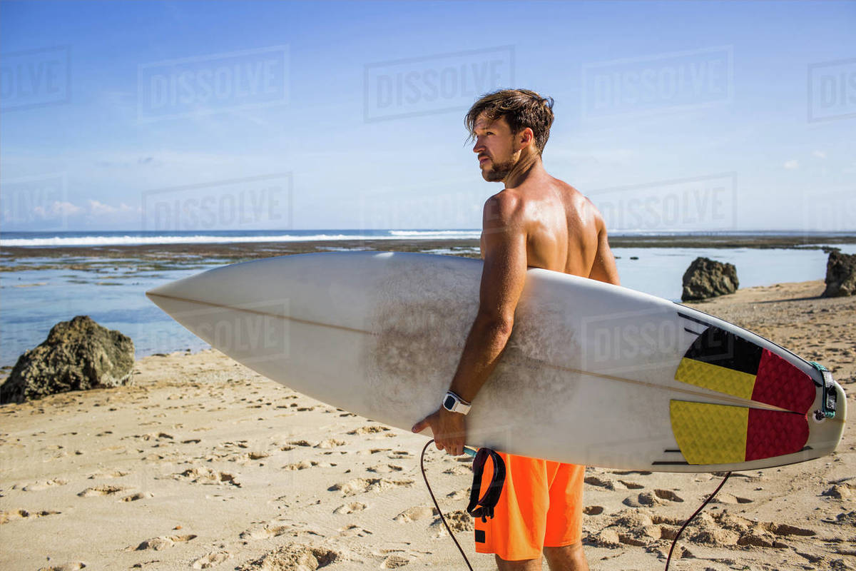 Side view of young surfer with surfing board standing on sandy beach on ...