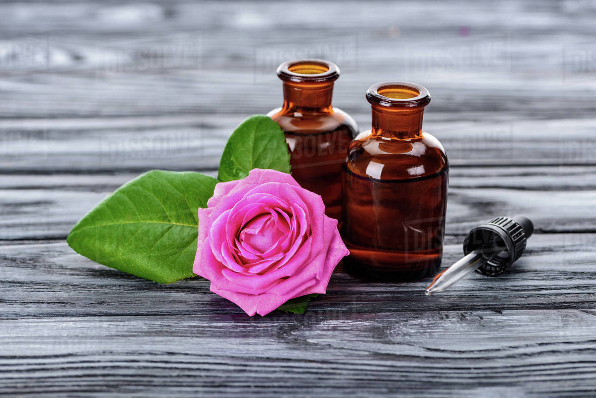 Bottles of natural herbal essential oils, pipette and pink rose on ...