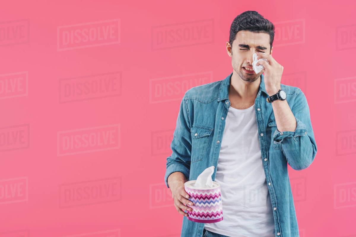 Sad young man with tissue box crying and wiping tears isolated on pink ...