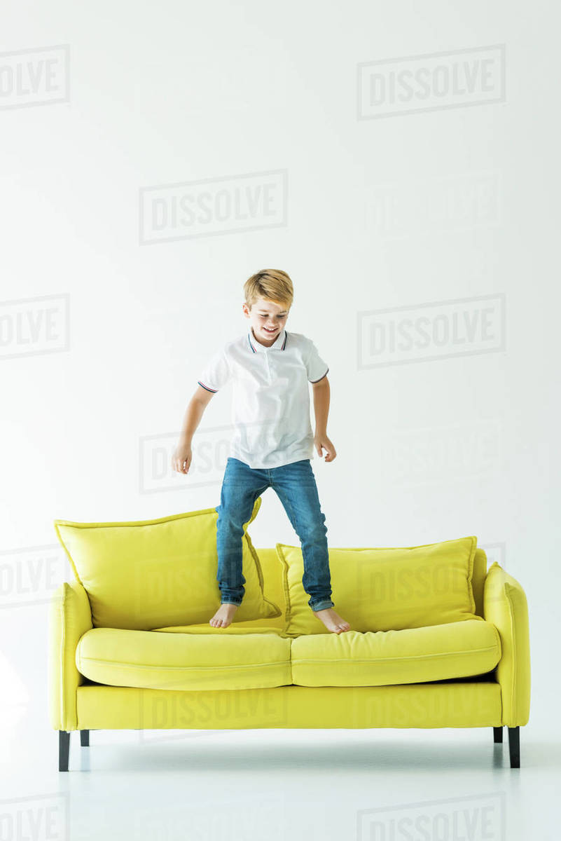 Happy adorable boy jumping on yellow sofa on white - Royalty-free Stock ...