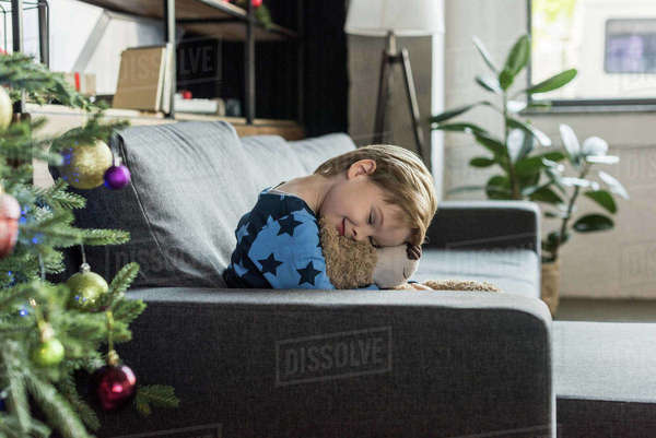 Side view of cute smiling kid sitting in sofa and sleeping with teddy ...