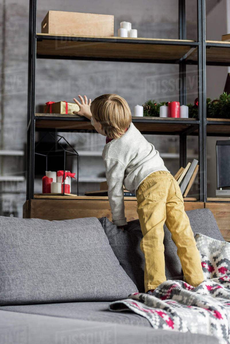Back view of child standing on couch and reaching for christmas gift ...