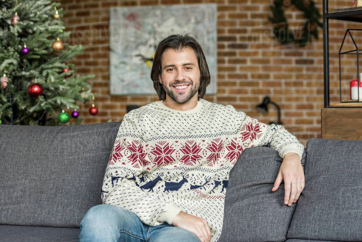 Handsome happy man sitting on couch and smiling at camera at christmas ...