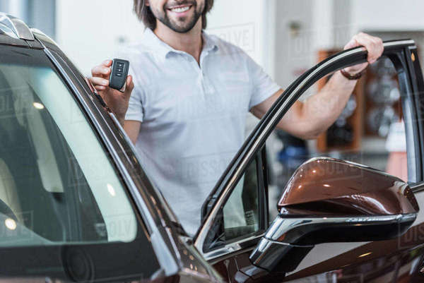 Cropped shot of smiling man with car key standing at new car in ...