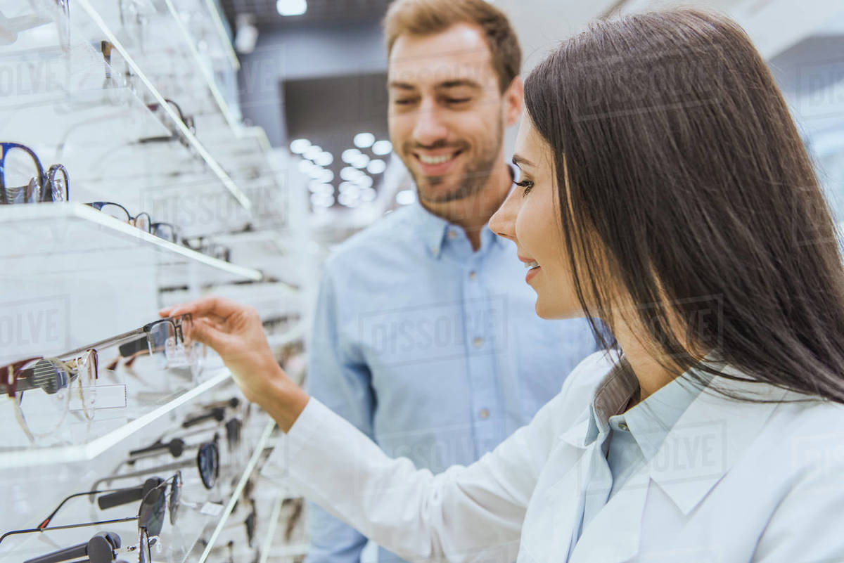 Selective focus of female oculist showing eyeglasses on shelves to ...