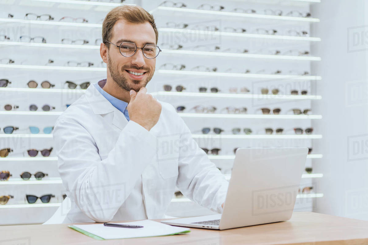 Professional optician using laptop at table with papers in ophthalmic ...