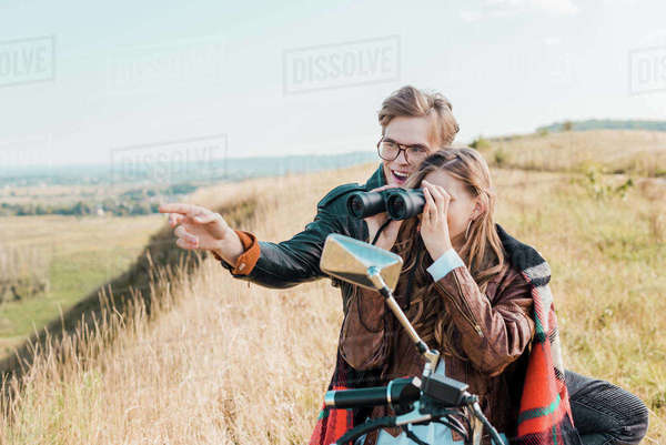 Girlfriend looking through binoculars near smiling boyfriend showing on ...
