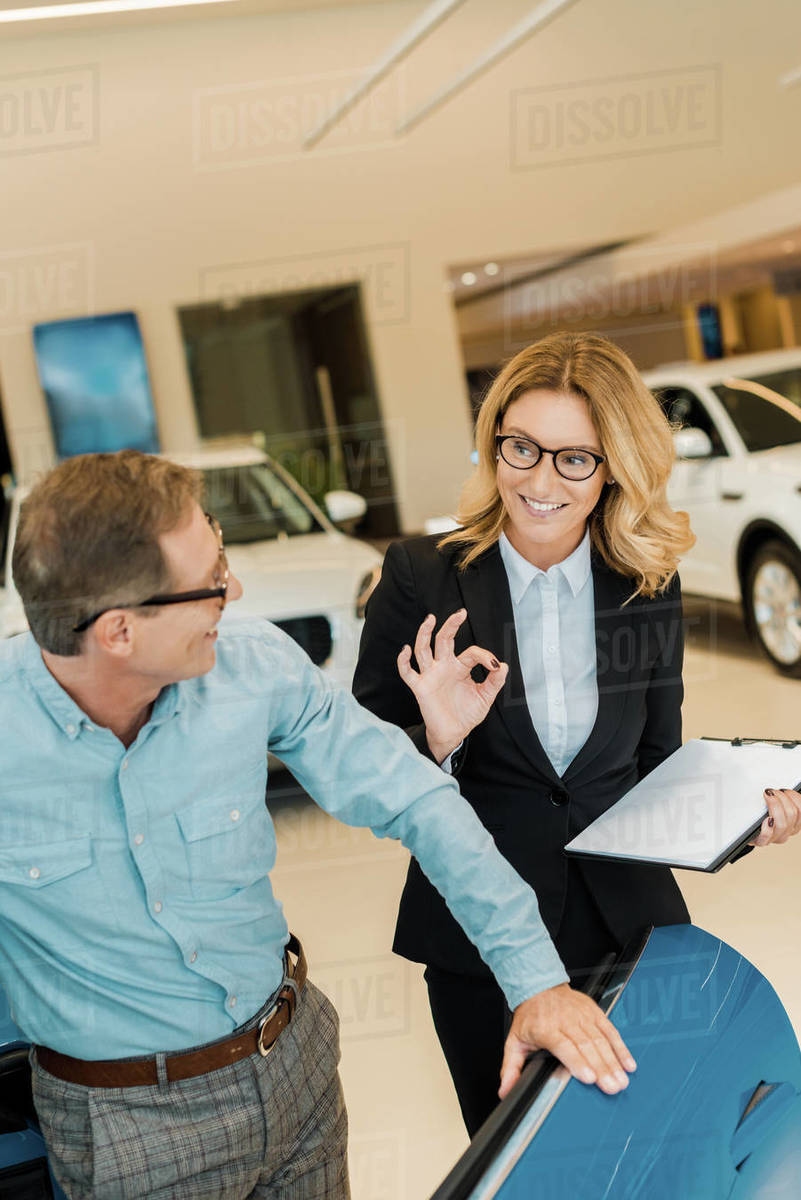 Adult man checking luxury sport car with female car dealer at showroom ...