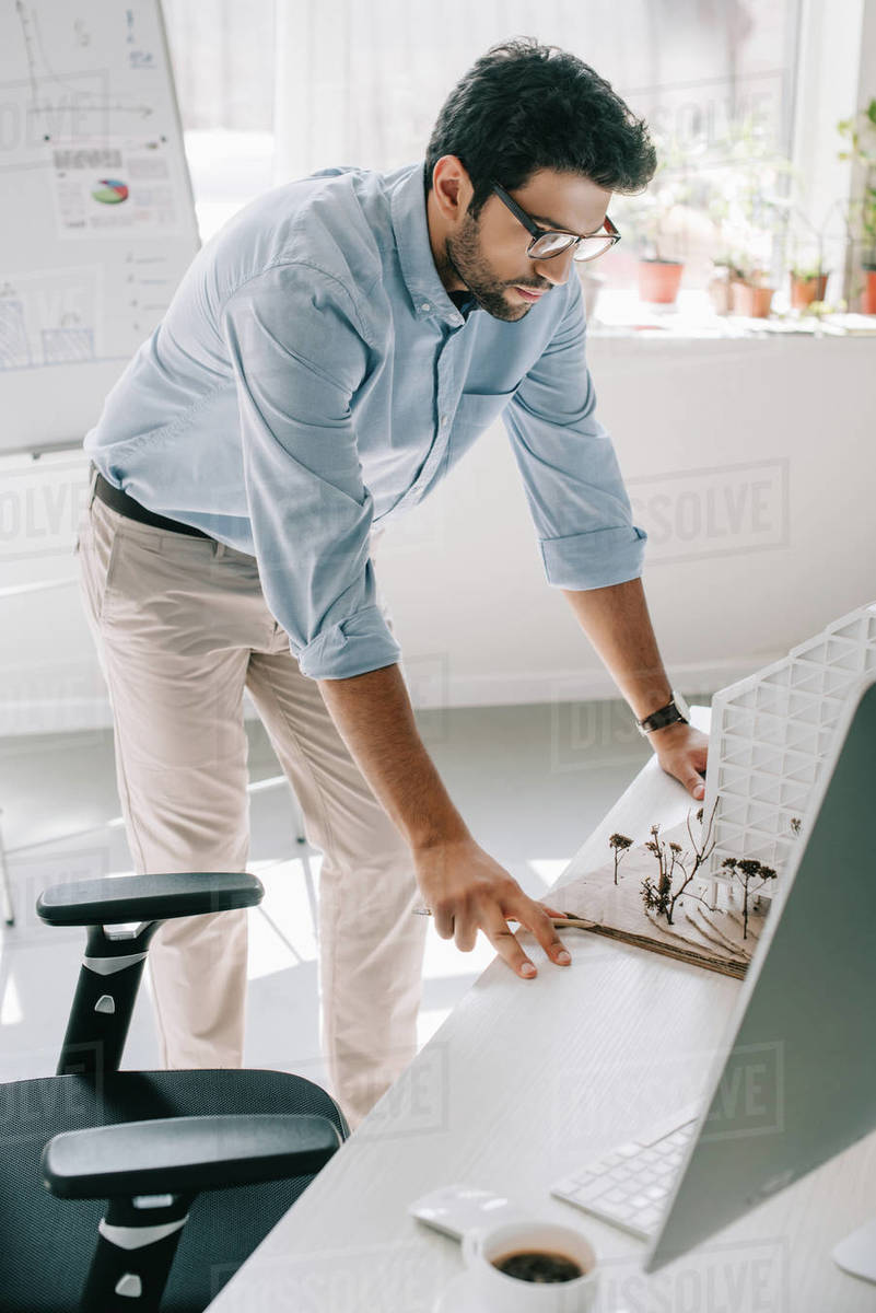 Handsome architect leaning on table and looking at architecture model ...