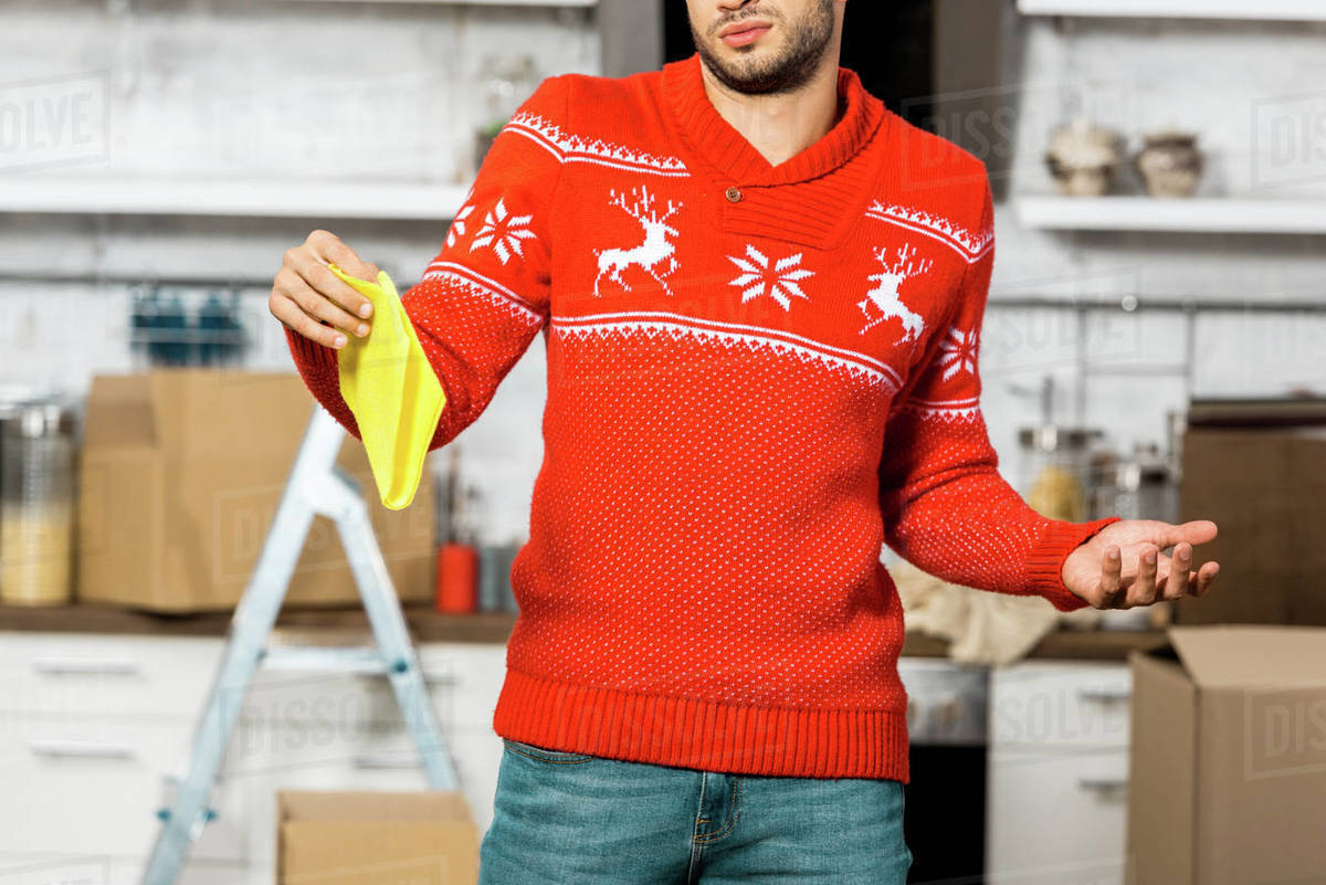 young man holding yellow dirty rag and doing shrug gesture in kitchen ...