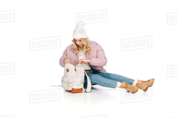 beautiful young woman in hat sitting and looking into backpack isolated ...