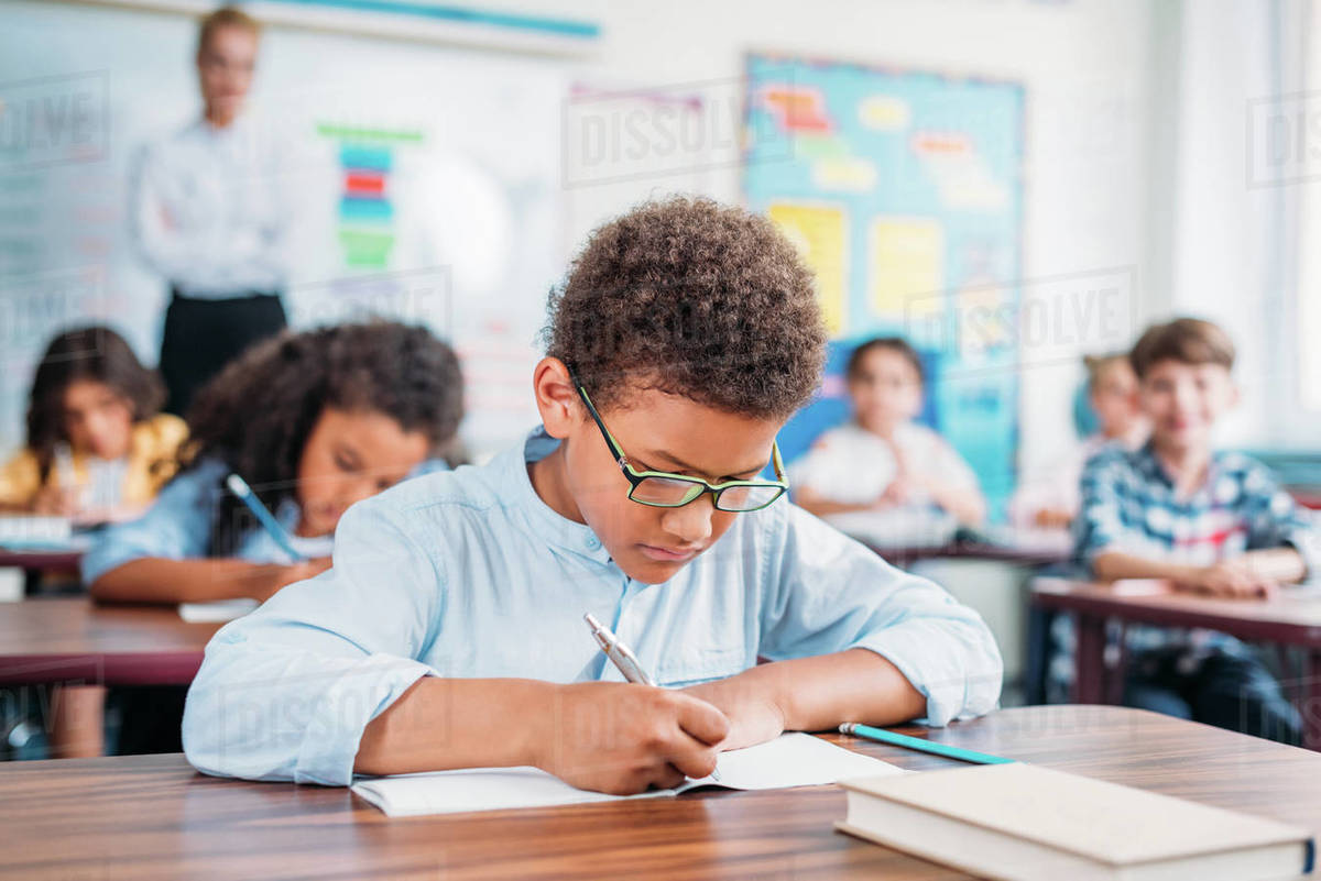 african american schoolboy writing in notebook at school - Royalty-free ...