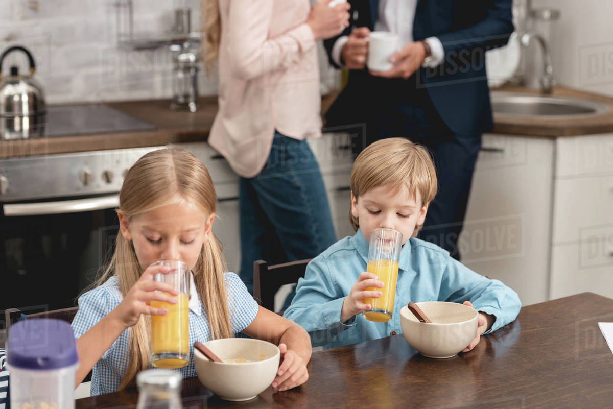 adorable little kids having breakfast together at kitchen while parents ...