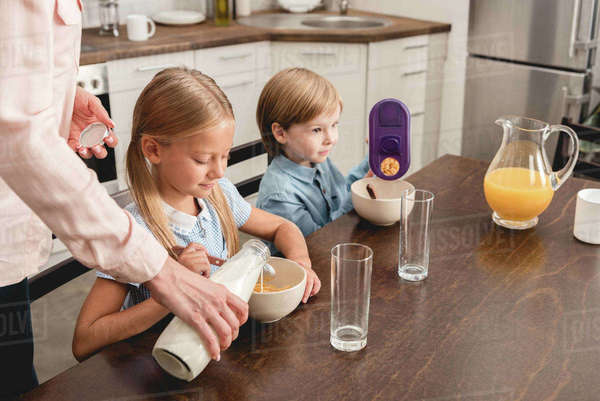 cropped shot of mother pouring milk into cereal for adorable little ...