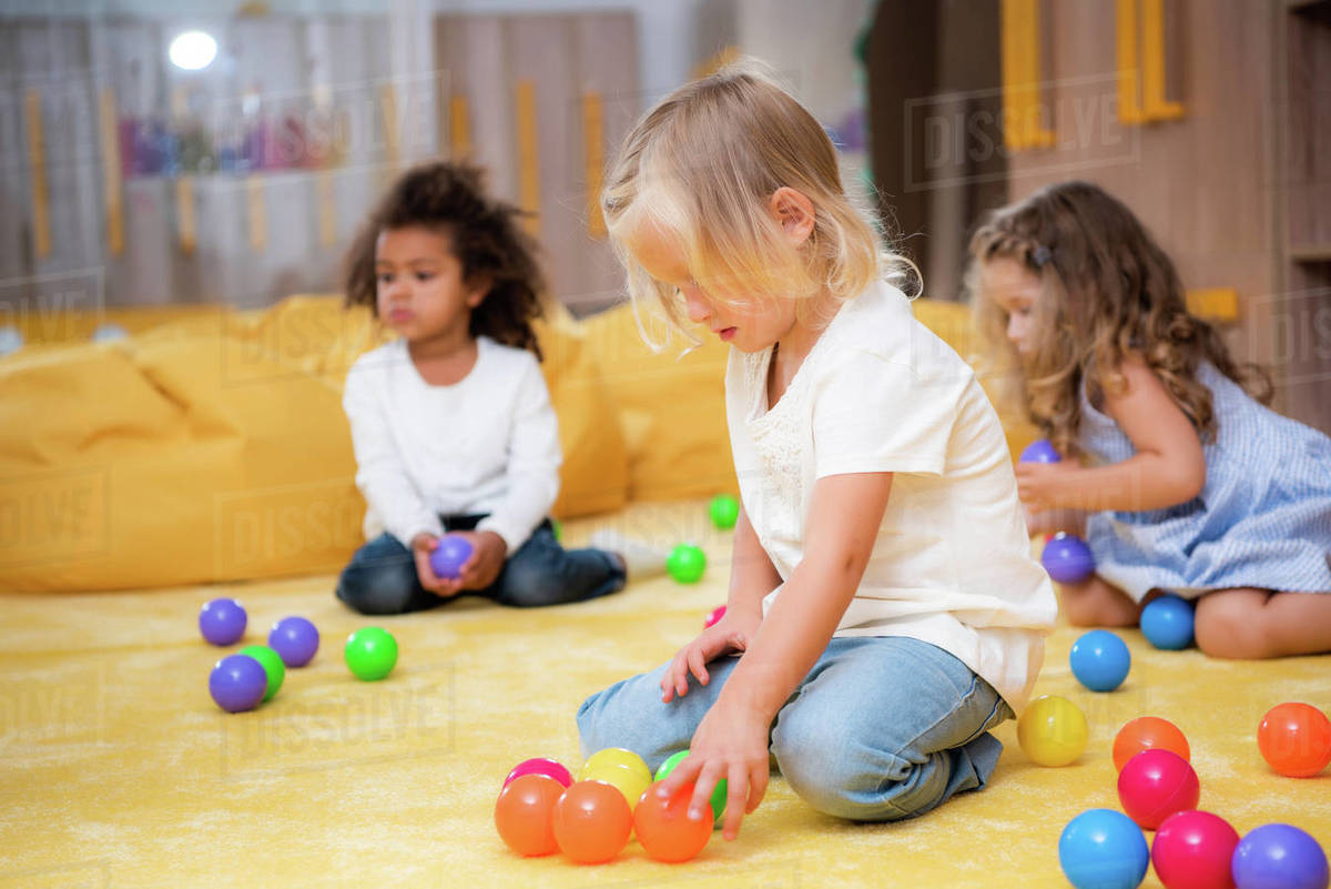 Adorable multiethnic children playing with colored balls on floor in ...