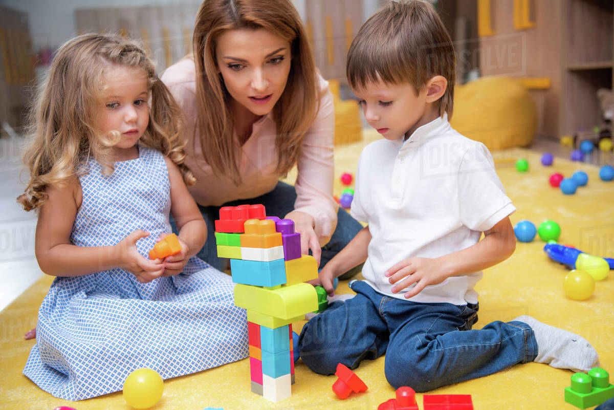 Educator and adorable kids playing with constructor in kindergarten ...