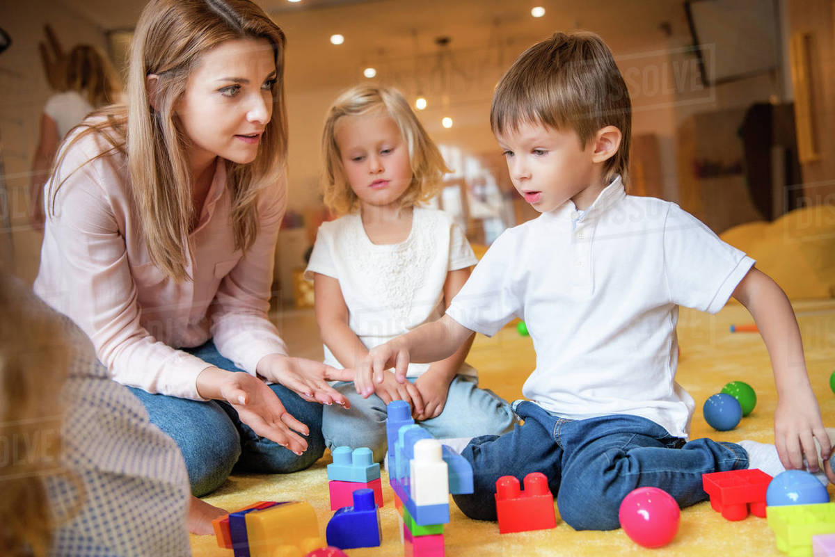 Educator and caucasian kids playing with constructor in kindergarten ...