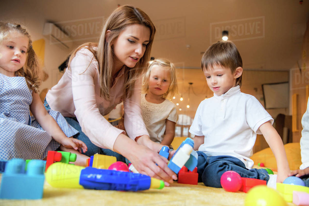 Educator helping kids playing with constructor in kindergarten ...