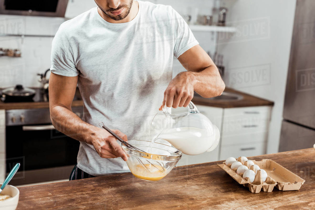 Cropped shot of young man pouring milk and cooking omelette at morning ...