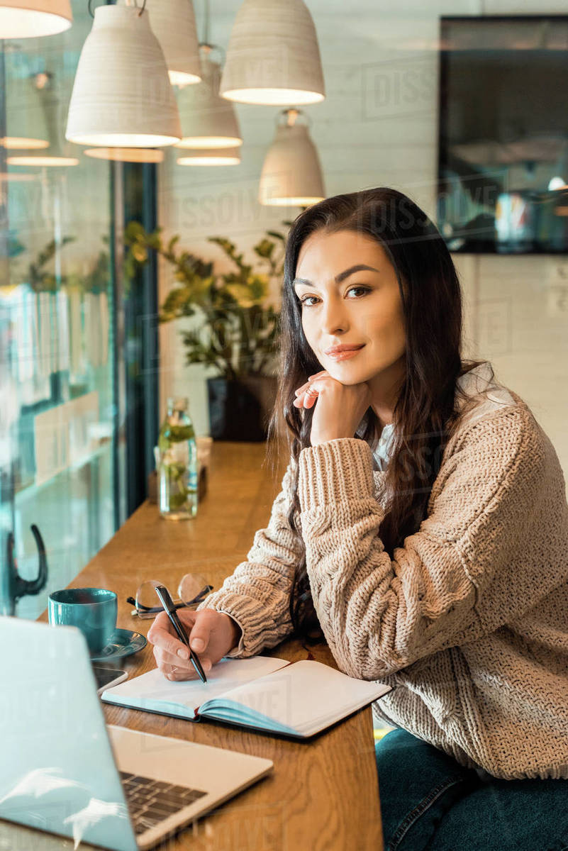 Beautiful female freelancer working with planner and laptop in cafe ...