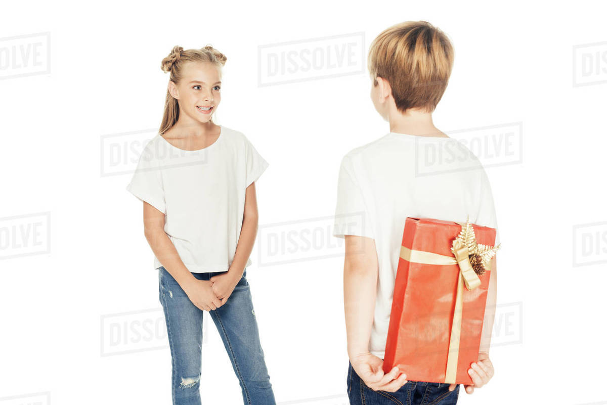Boy hiding gift box behind back to present to friend isolated on white ...