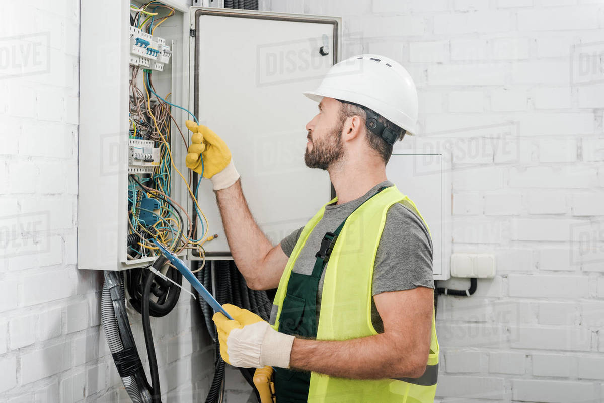 Side view of electrician holding clipboard and checking wires in ...