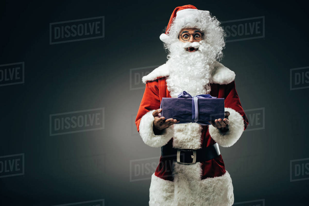Surprised Santa Claus in costume holding gift box isolated on grey ...
