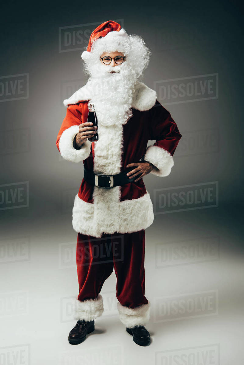 Happy Santa Claus in costume standing with cream soda bottle on grey ...