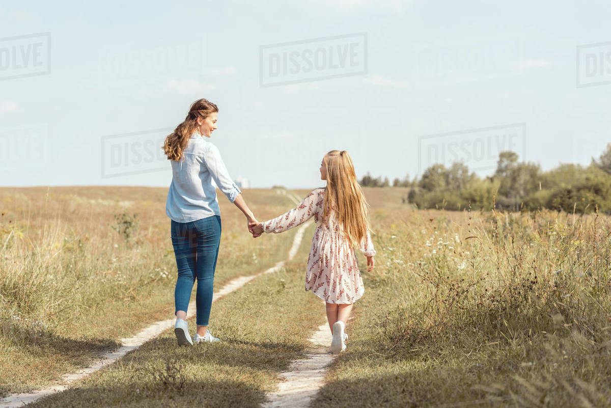 Rear View Of Mother And Daughter Holding Hands And Walking Together In