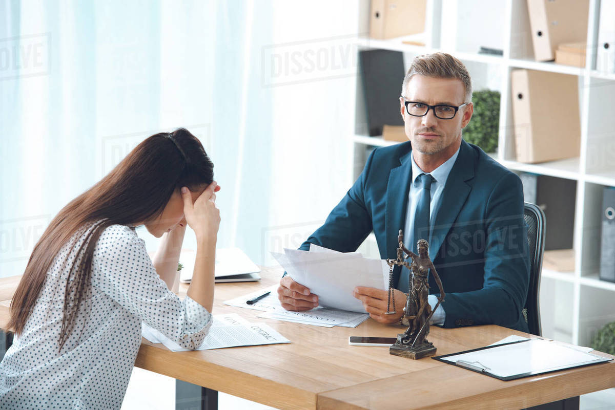 Lawyer holding papers and looking at camera while sad female client ...