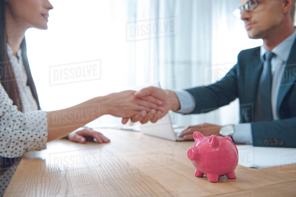 Selective focus of insurance agent and client shaking hands at tabletop ...