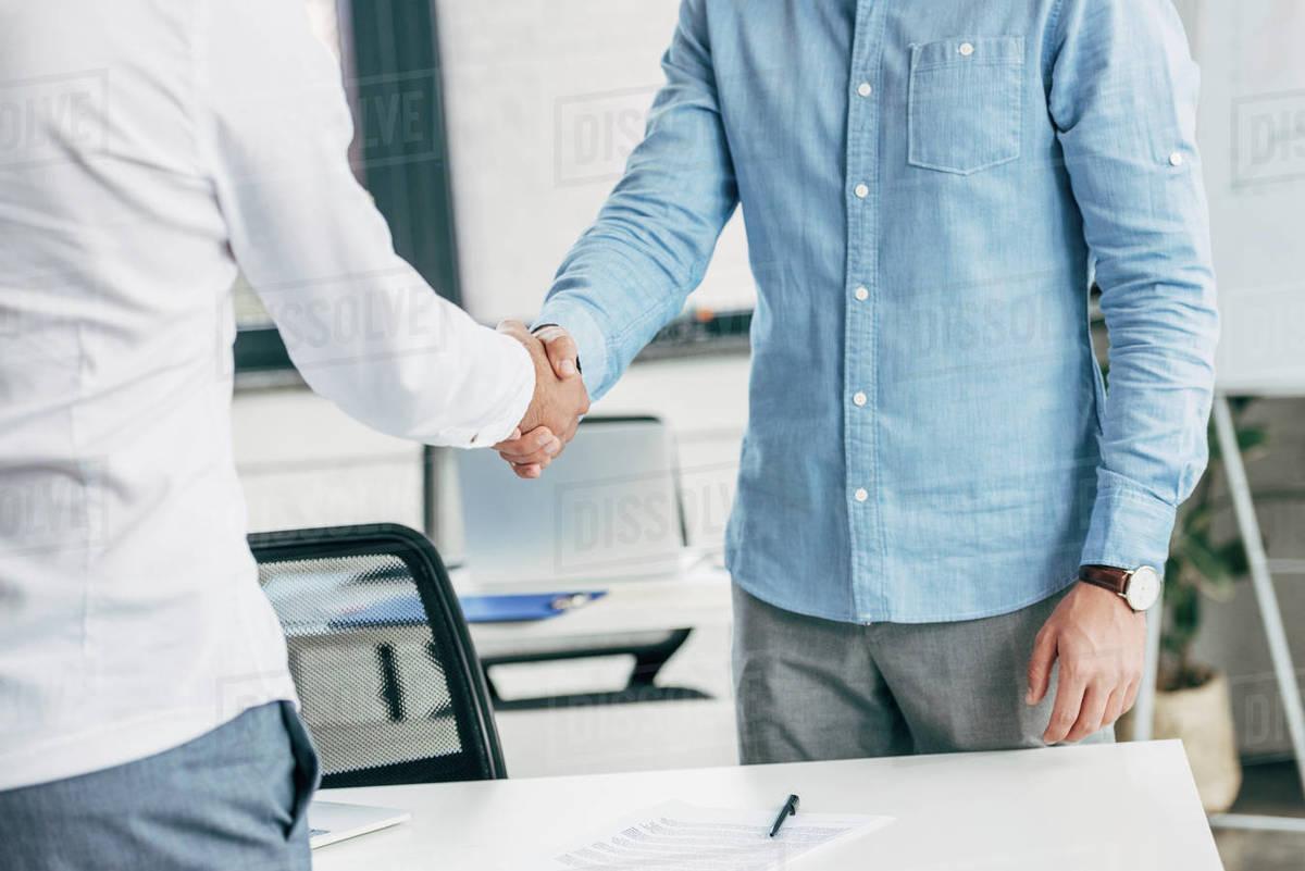 cropped shot of businessmen shaking hands at workplace - Royalty-free ...