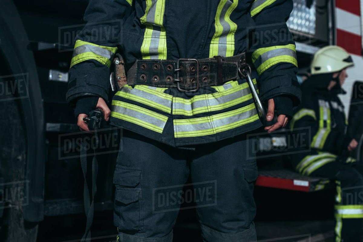 cropped shot of firefighter in fireproof uniform and colleague behind ...
