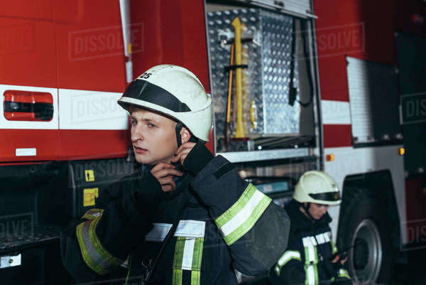 firefighter checking helmet with colleague behind at fire department ...
