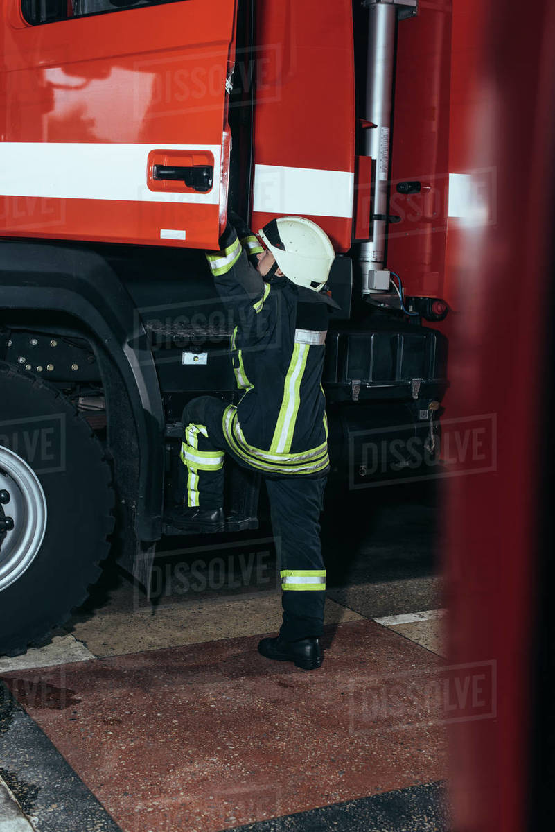 female firefighter in protective uniform getting into truck at fire ...