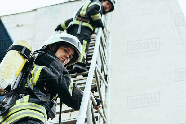 low angle view of firefighters in helmets standing on ladder and ...