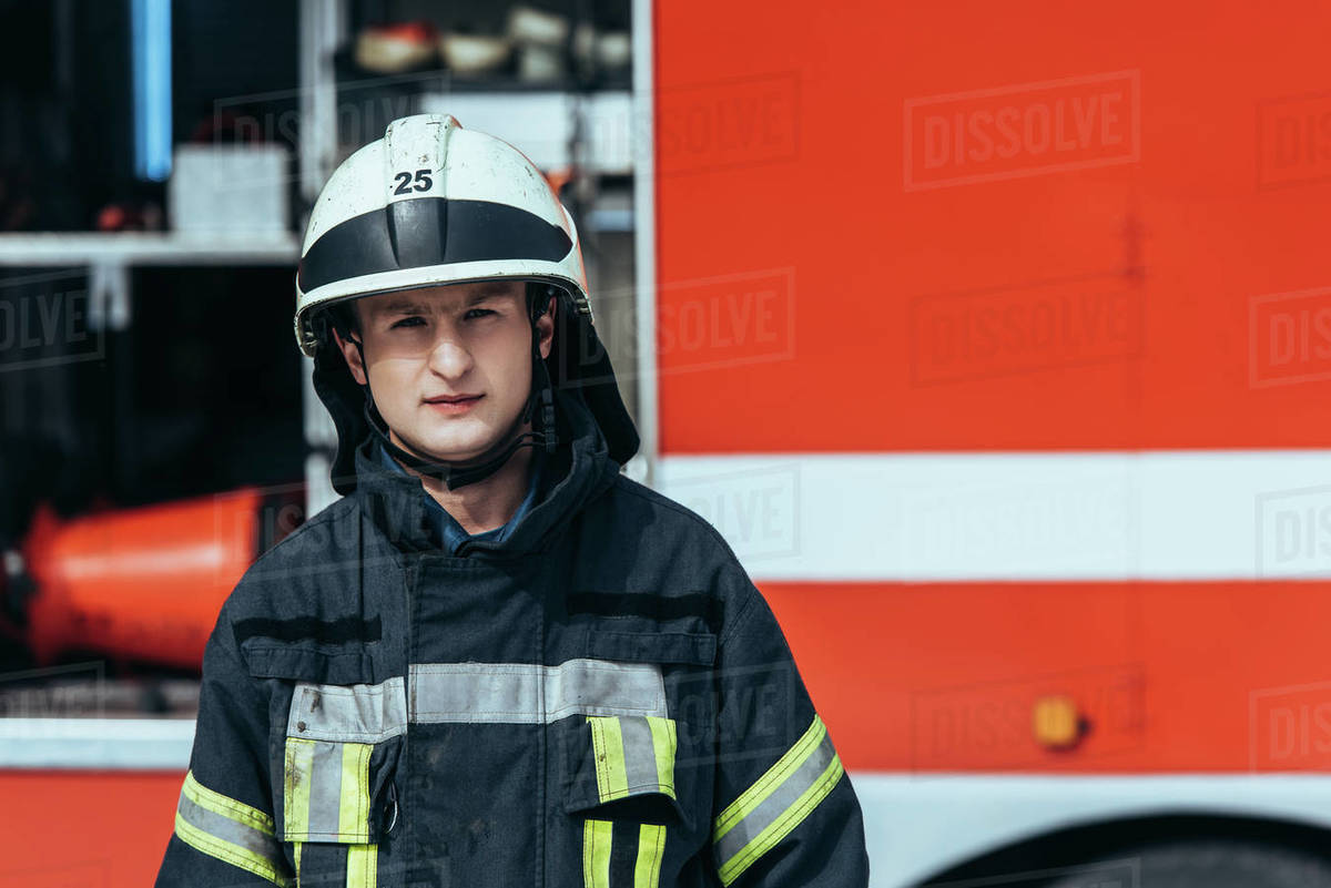 portrait of firefighter in uniform standing on street with red fire ...