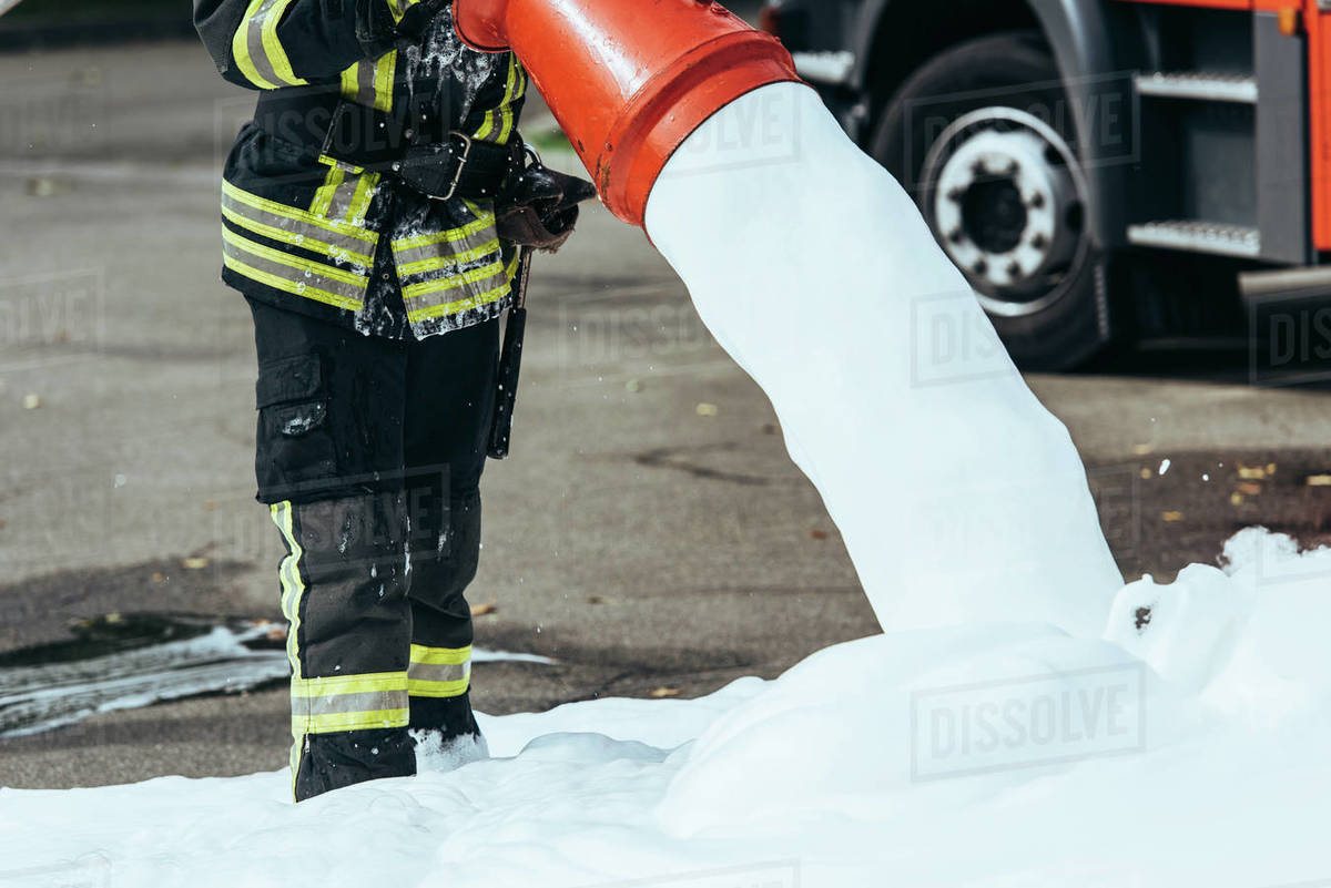 cropped shot of firefighter extinguishing fire with foam on street ...