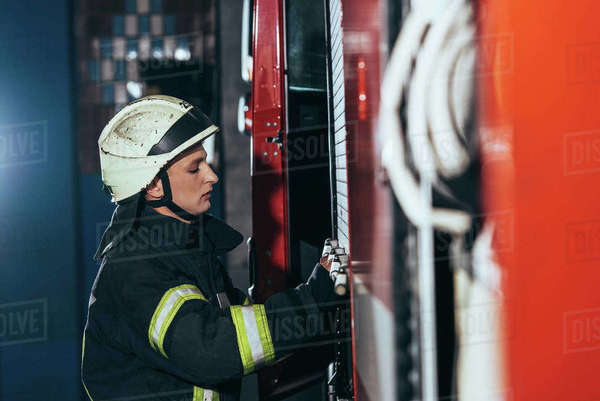 side view of fireman in uniform closing truck at fire department ...